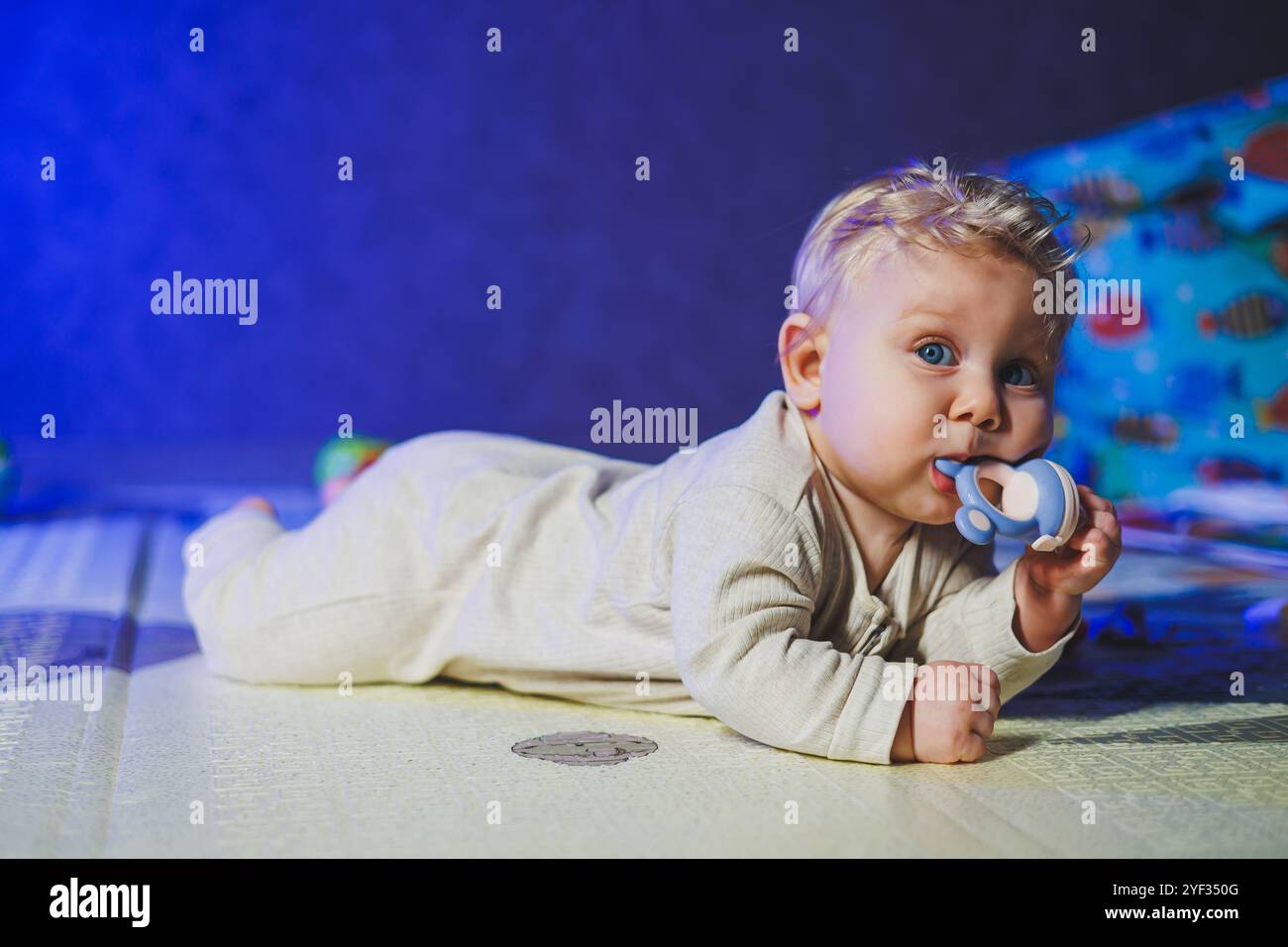 A 6-month-old child is lying on a mat and biting a rodent. A teether in ...