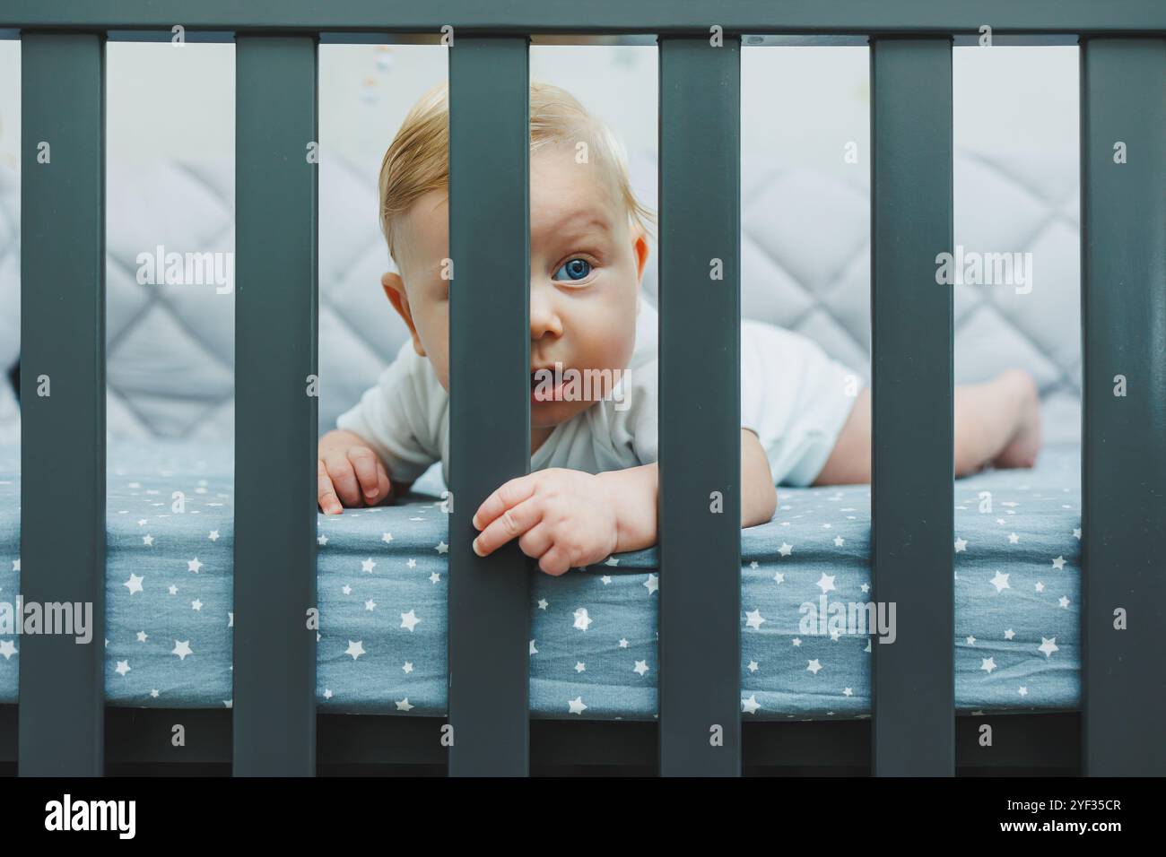 The baby looks through the sides of the crib into the room. A small ...