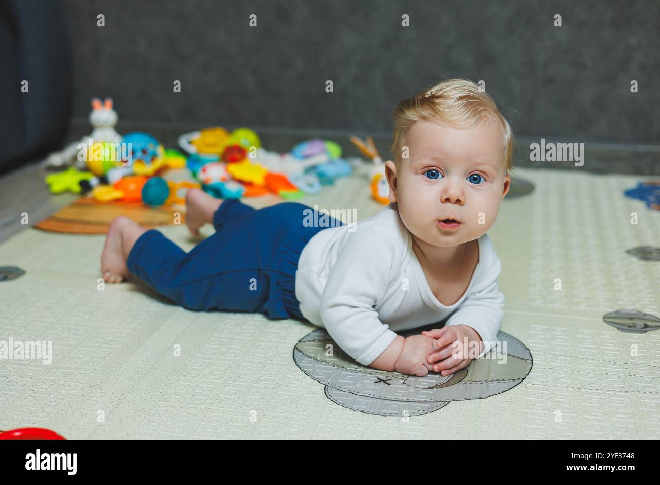 A blue-eyed baby is lying on the floor and holding his head ...