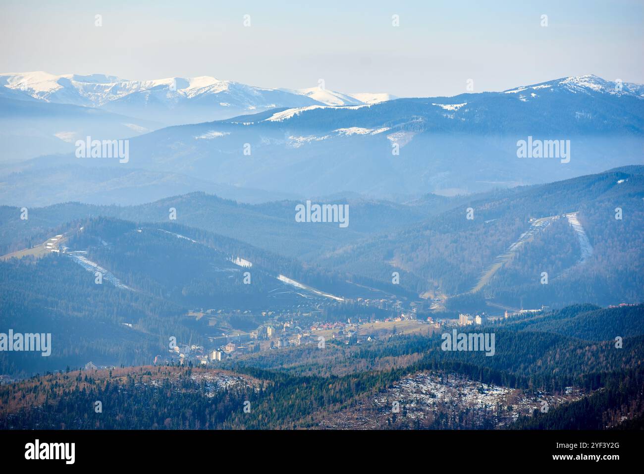Aerial view of layered mountain ranges partially covered in snow. Valleys filled with dense ...