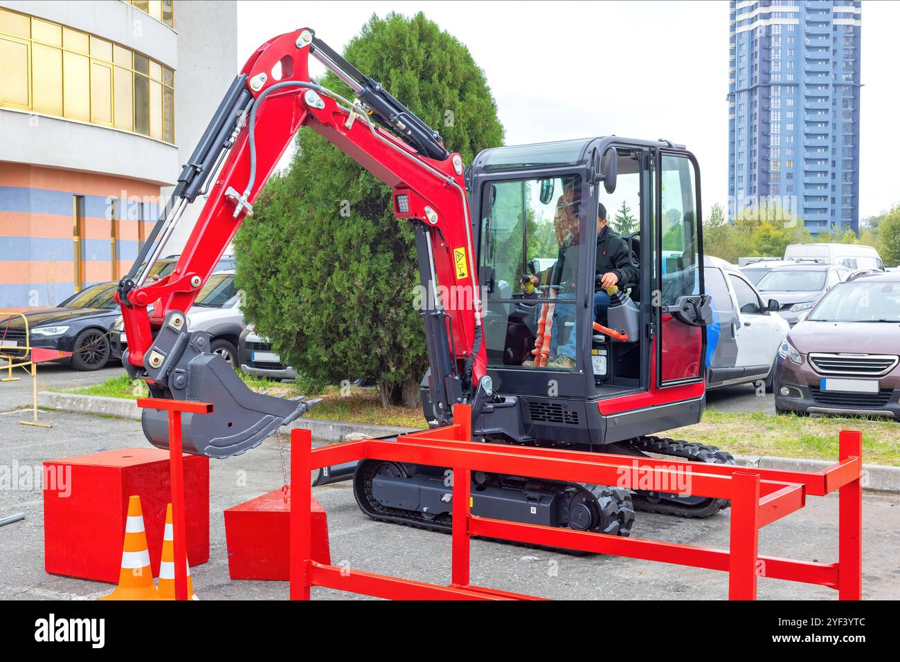 At construction site, a compact red excavator with operator visible and ...