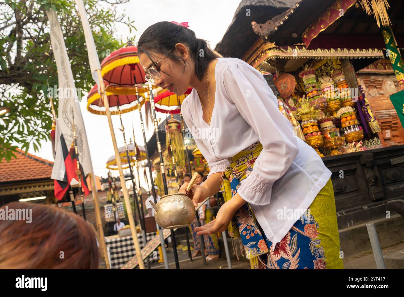 A Balinese Hindu female temple worker sprinkling water on visitors ...