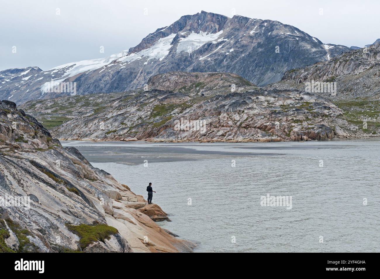 Inuit hunters fishing at the fjord in front of a mountainous landscape ...