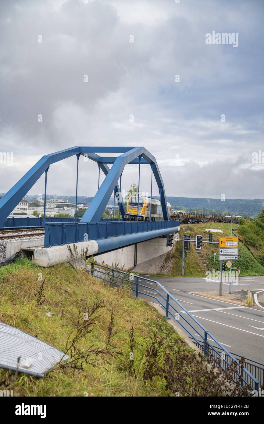 Yellow train crosses blue bridge above a road in rural surroundings ...