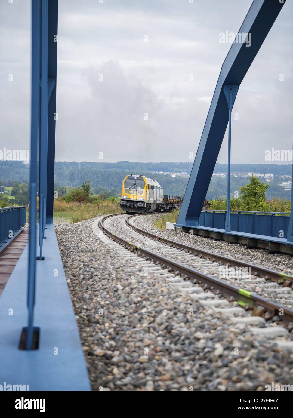 Train is on curved railway line, flanked by blue bridge, track ...