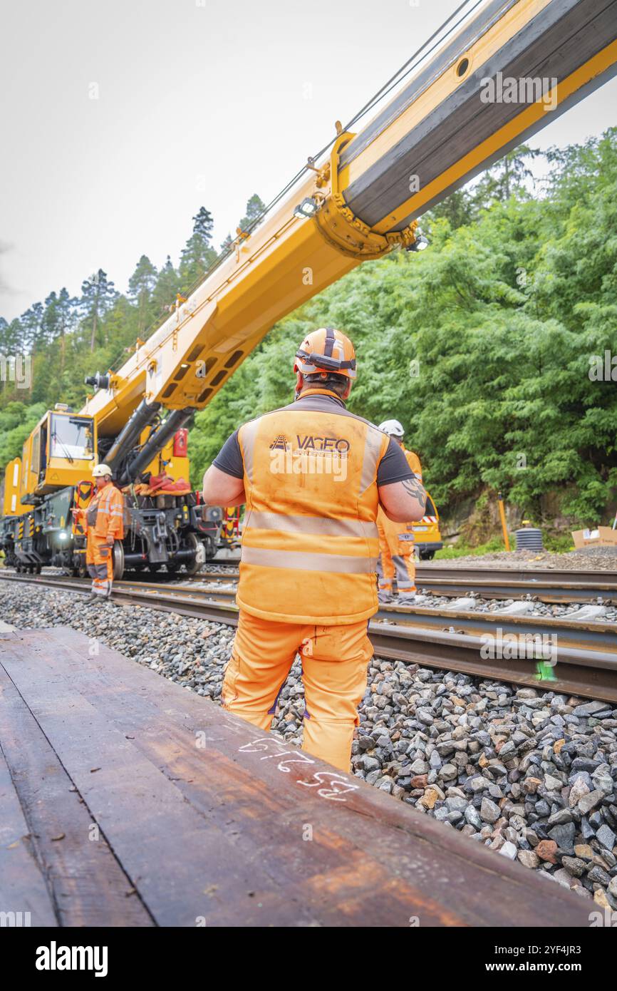 Construction worker in orange safety clothing stands on tracks while a ...
