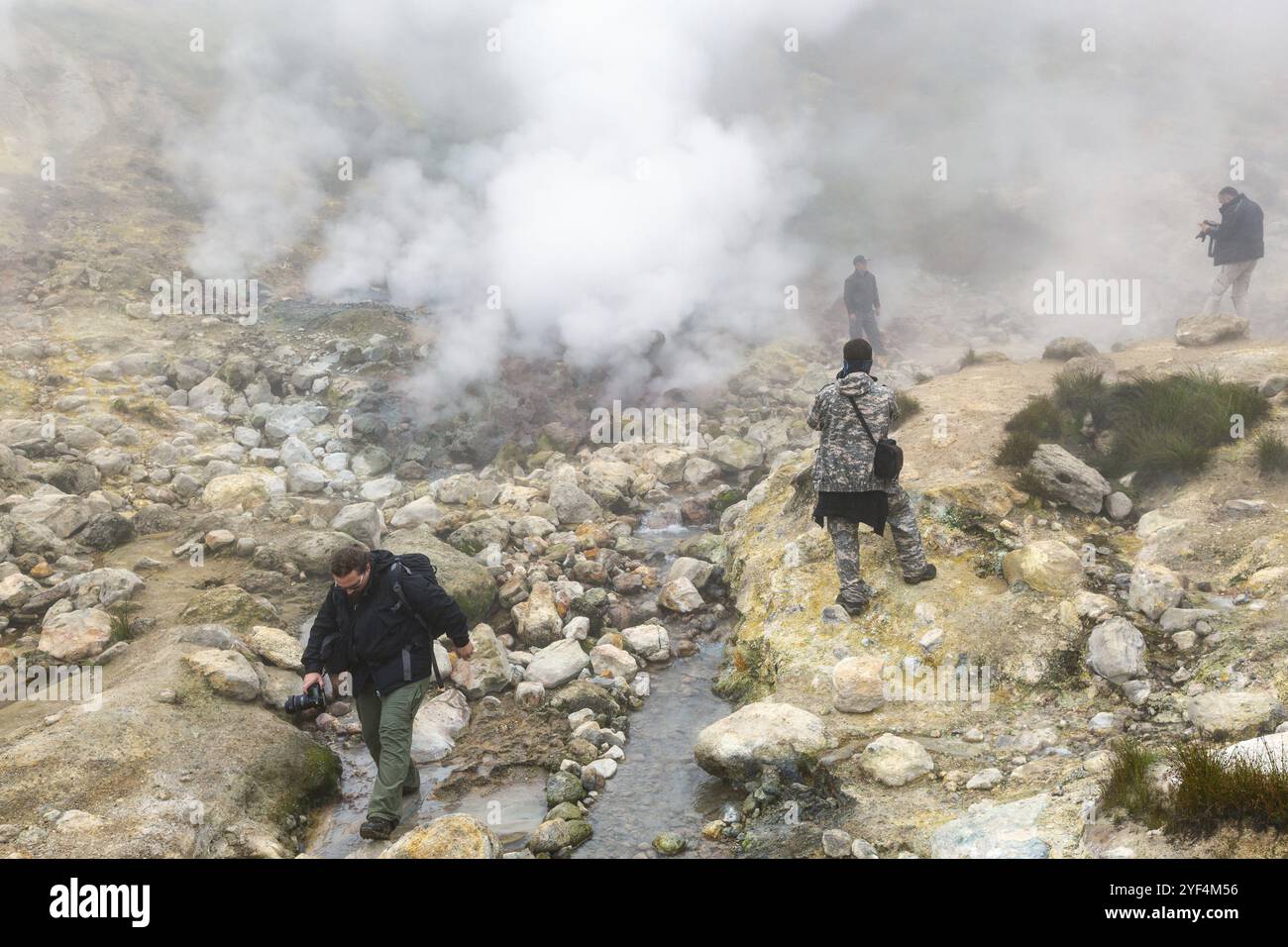 Group of travelers and photographer walks through volcanic landscape ...
