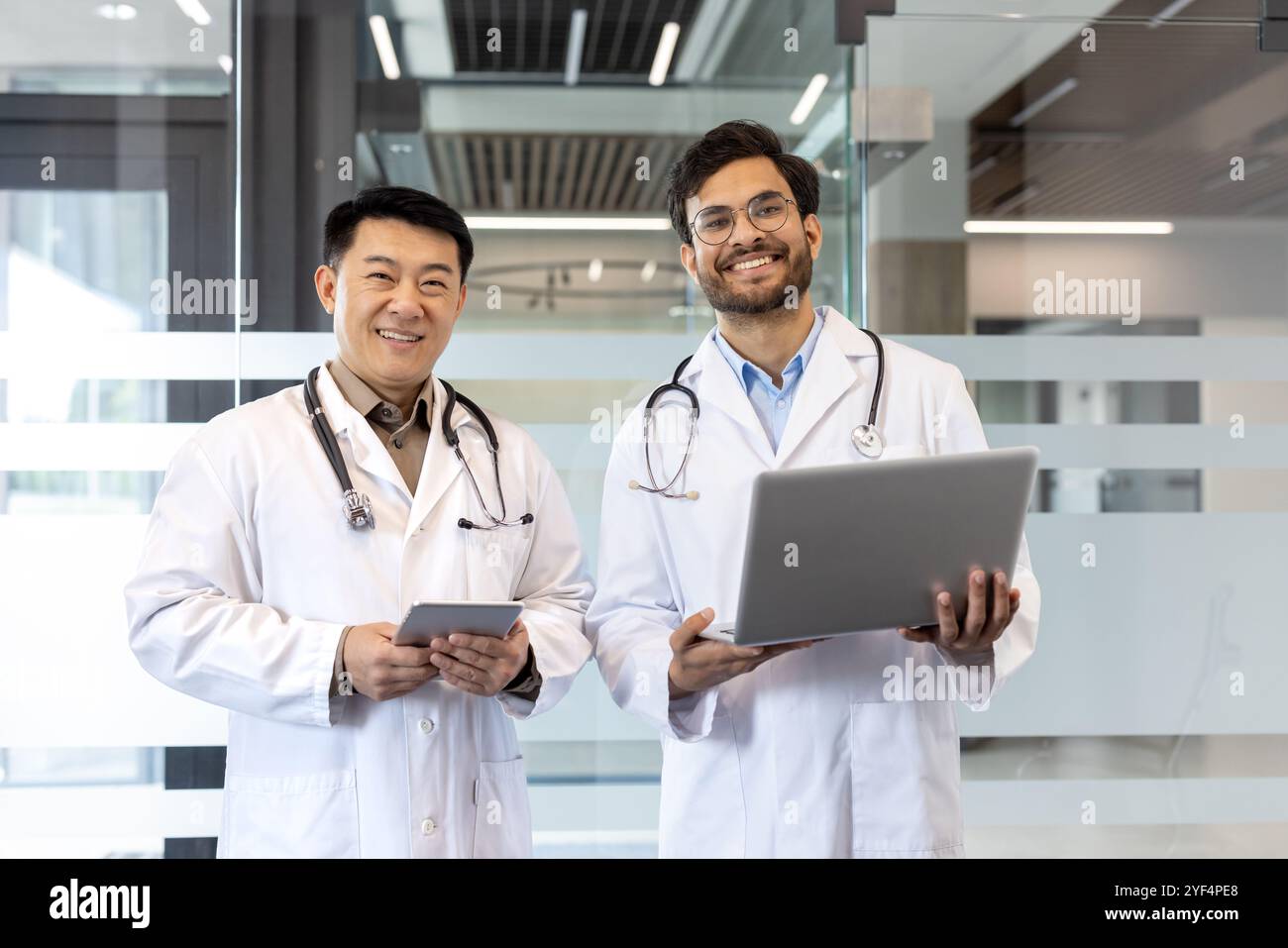 Doctors standing in office, one holding laptop, other with tablet ...