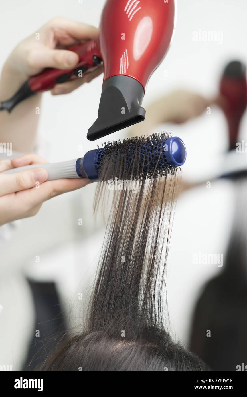 Hands of beautician drying long brunette hair of client using red hair ...