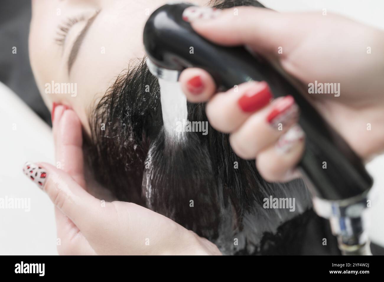 Hands of hairdresser wash long hair of brunette woman with shampoo ...
