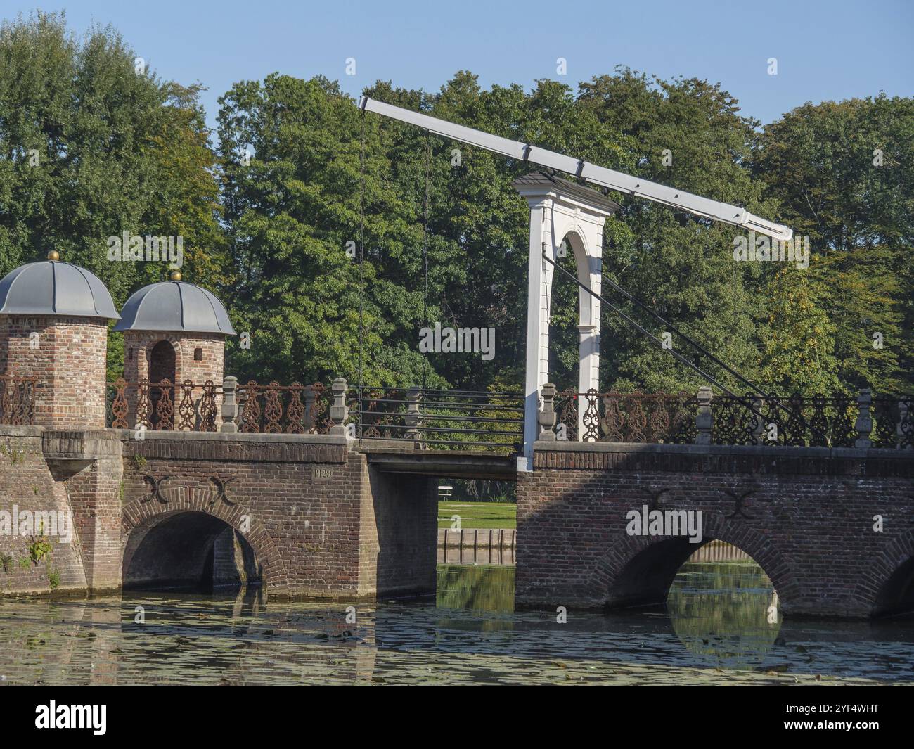 A wrought-iron bridge spans calm water, framed by trees, anholt ...
