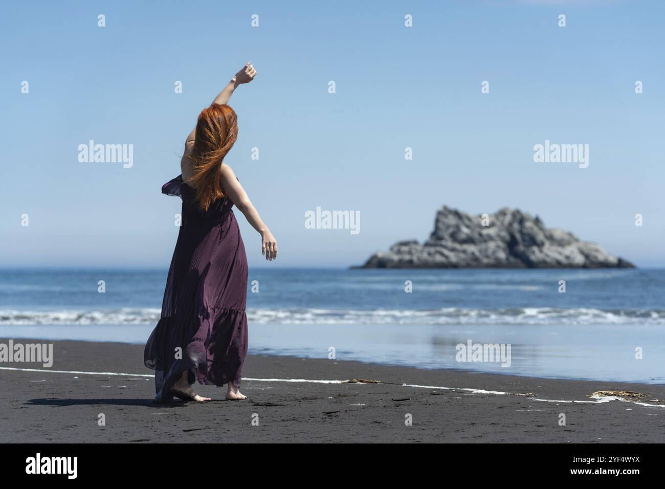 Unrecognizable redhead woman in dark puce long dress standing on sandy ...