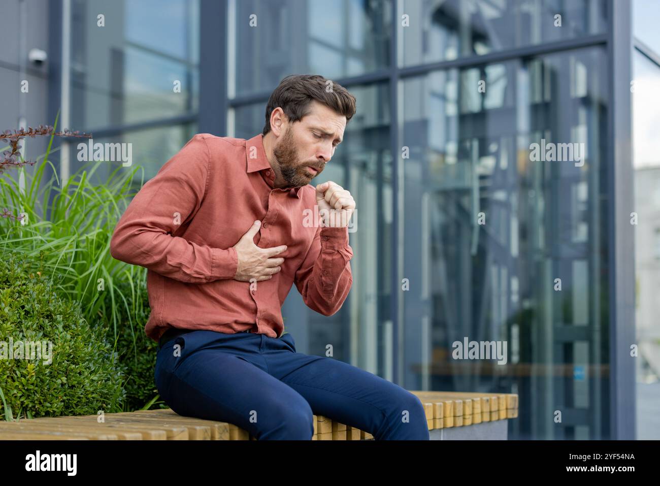 Mature man outdoors experiencing chest discomfort and cough. Seated ...