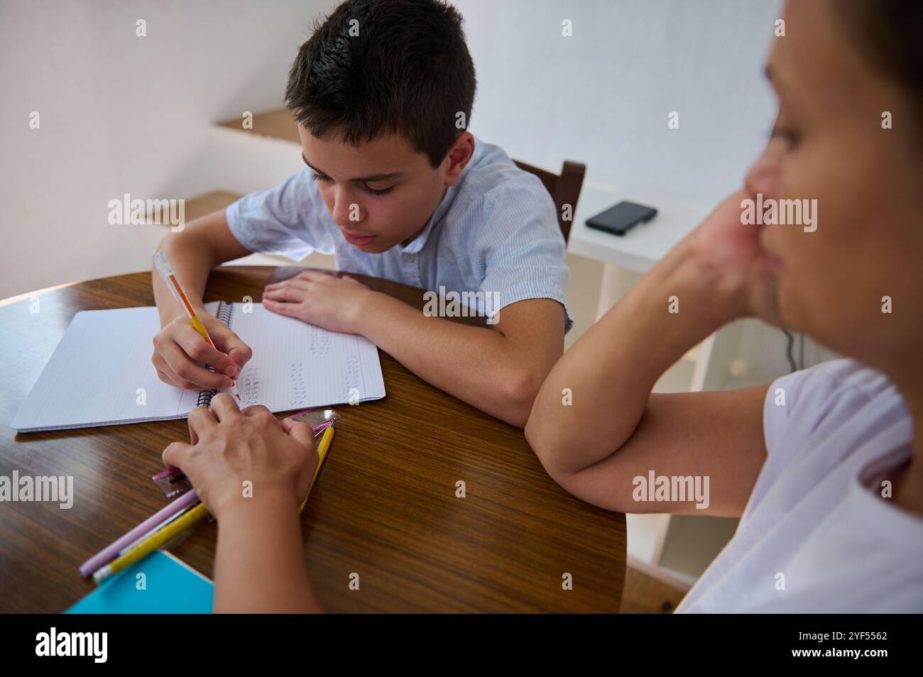 A caring mother assists her son with his homework at the dining table ...