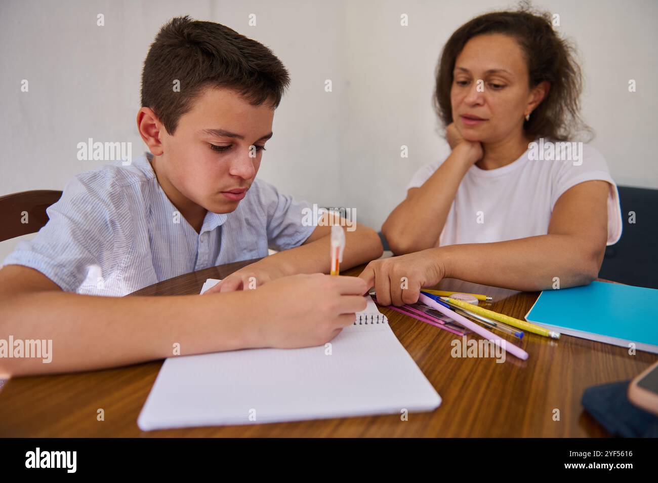 A focused boy works on homework under the guidance of his mother at the ...