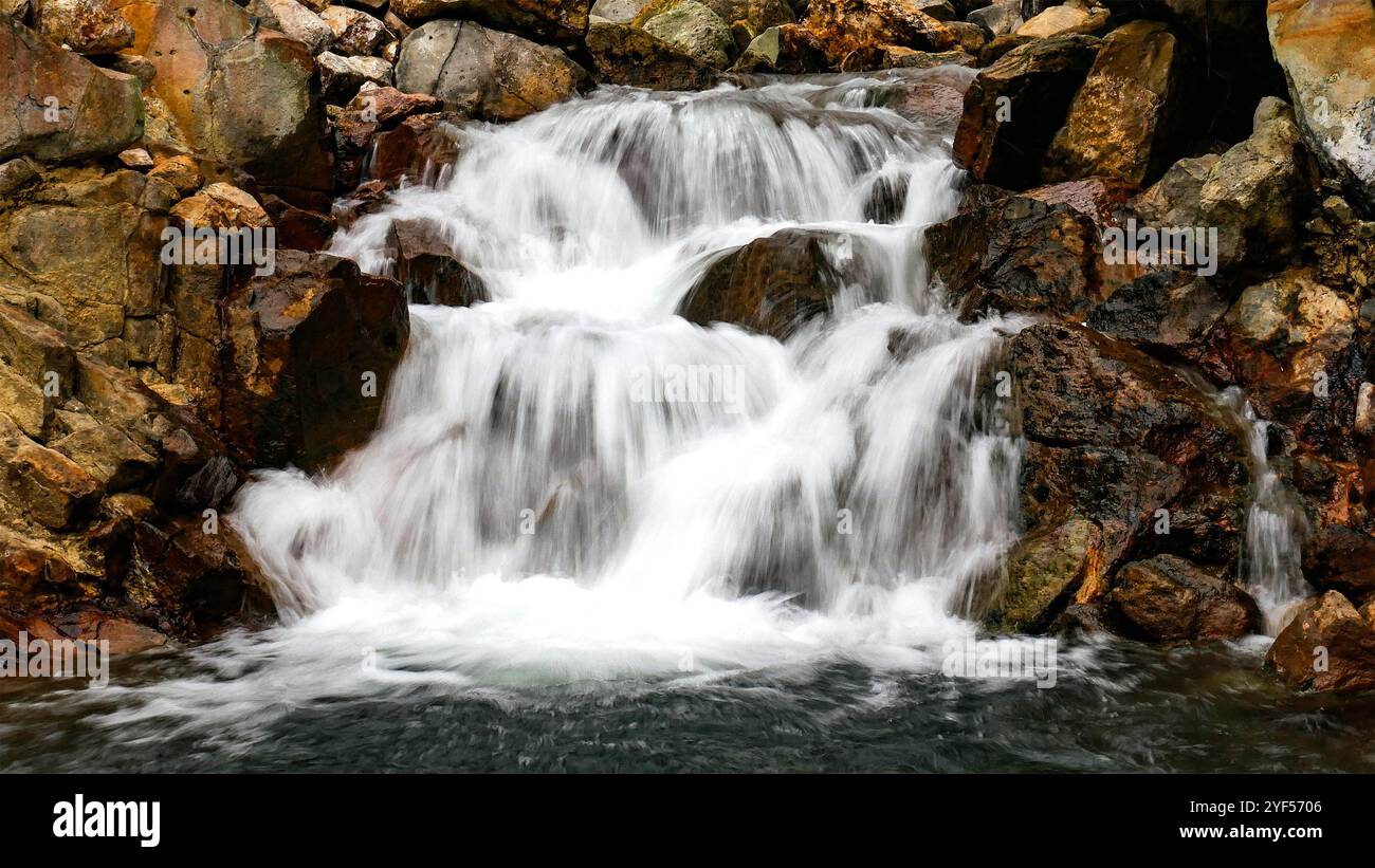 A small waterfall with clear water flows rapidly over large natural ...