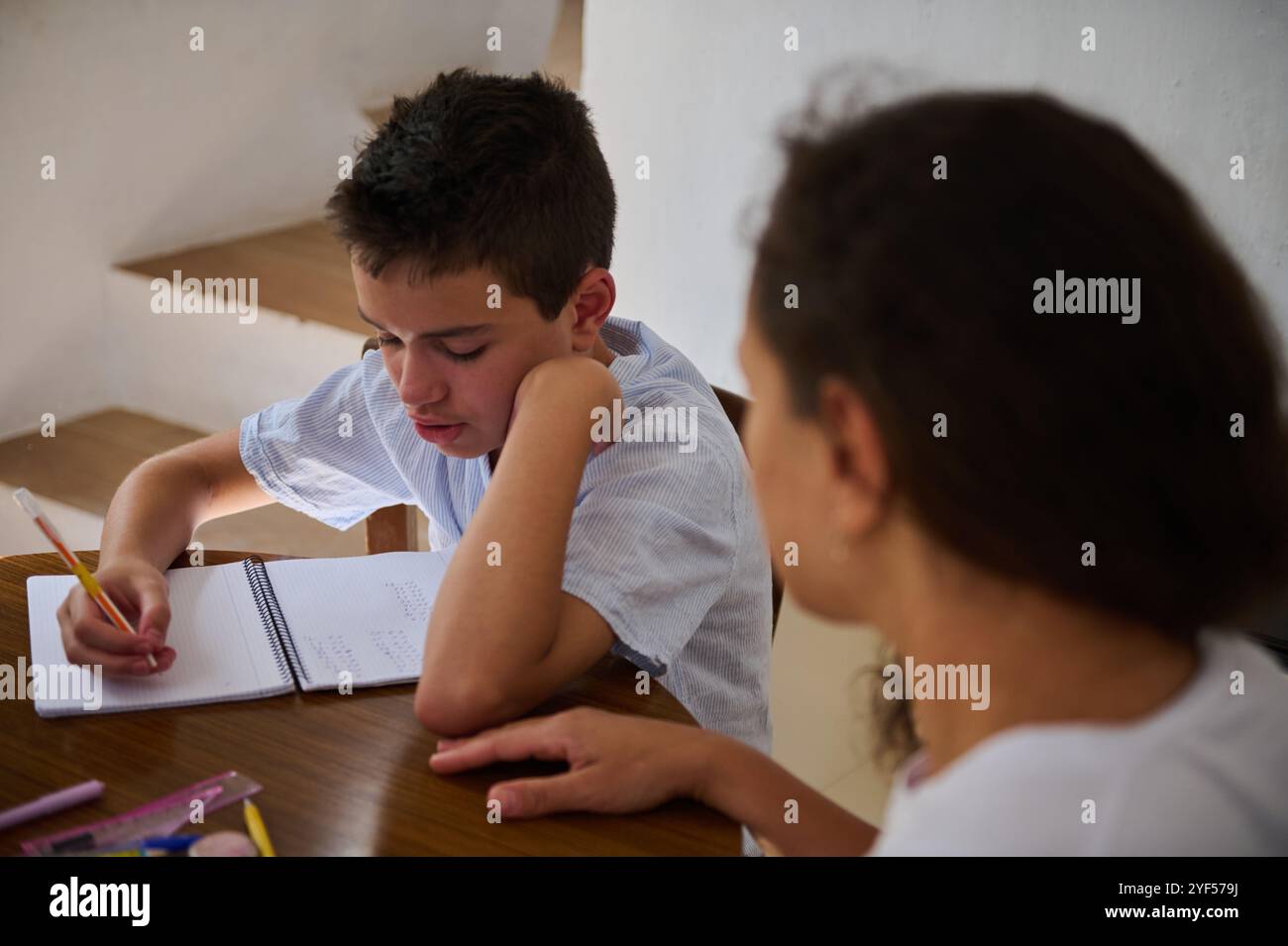 A focused boy works on his homework with his mother's help at the ...