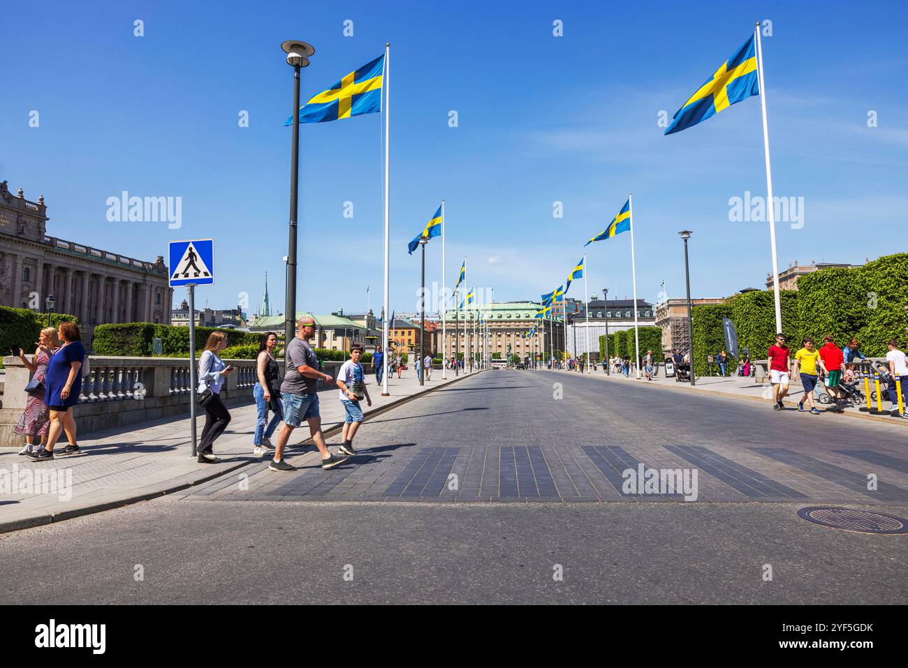 Pedestrians crossing street lined with Swedish flags near historic ...