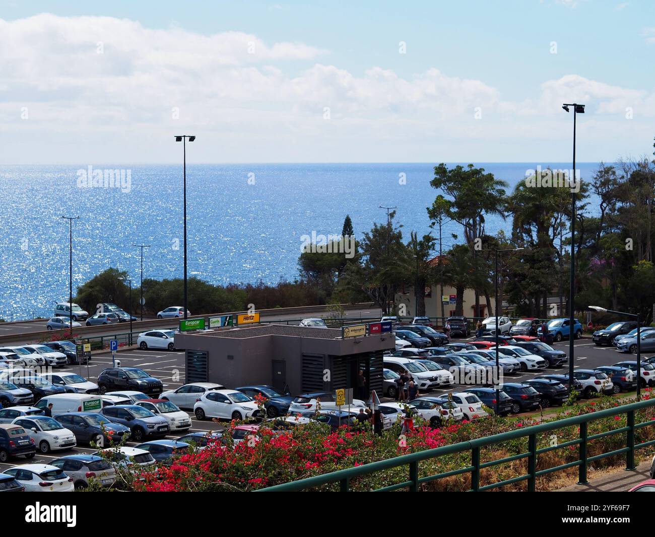 A busy parking lot filled with cars is situated by the ocean, with the ...
