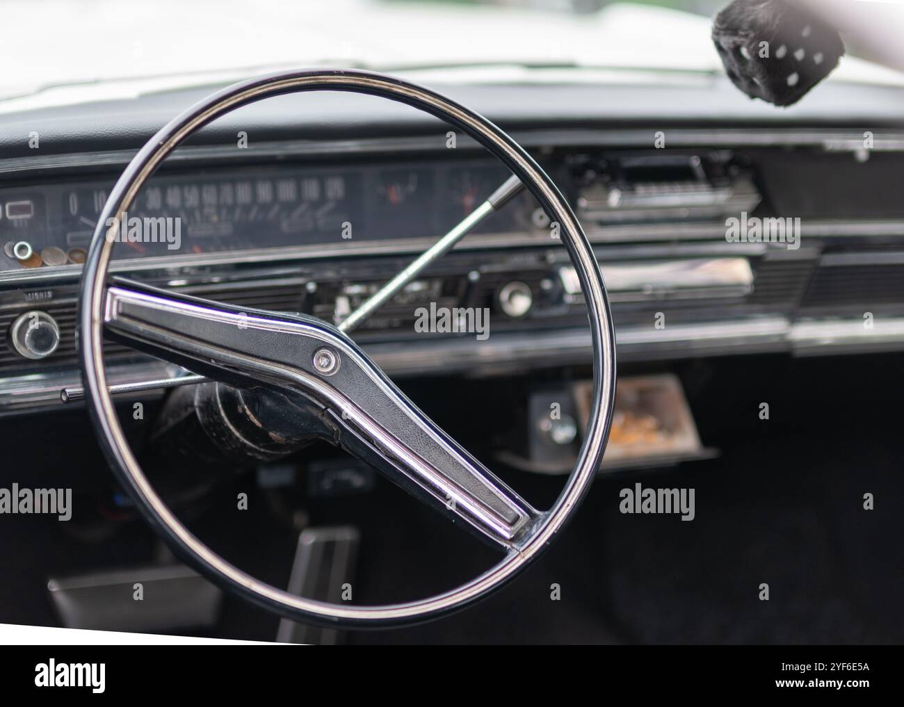 A close-up of a vintage car's steering wheel, with a fuzzy dice hanging ...