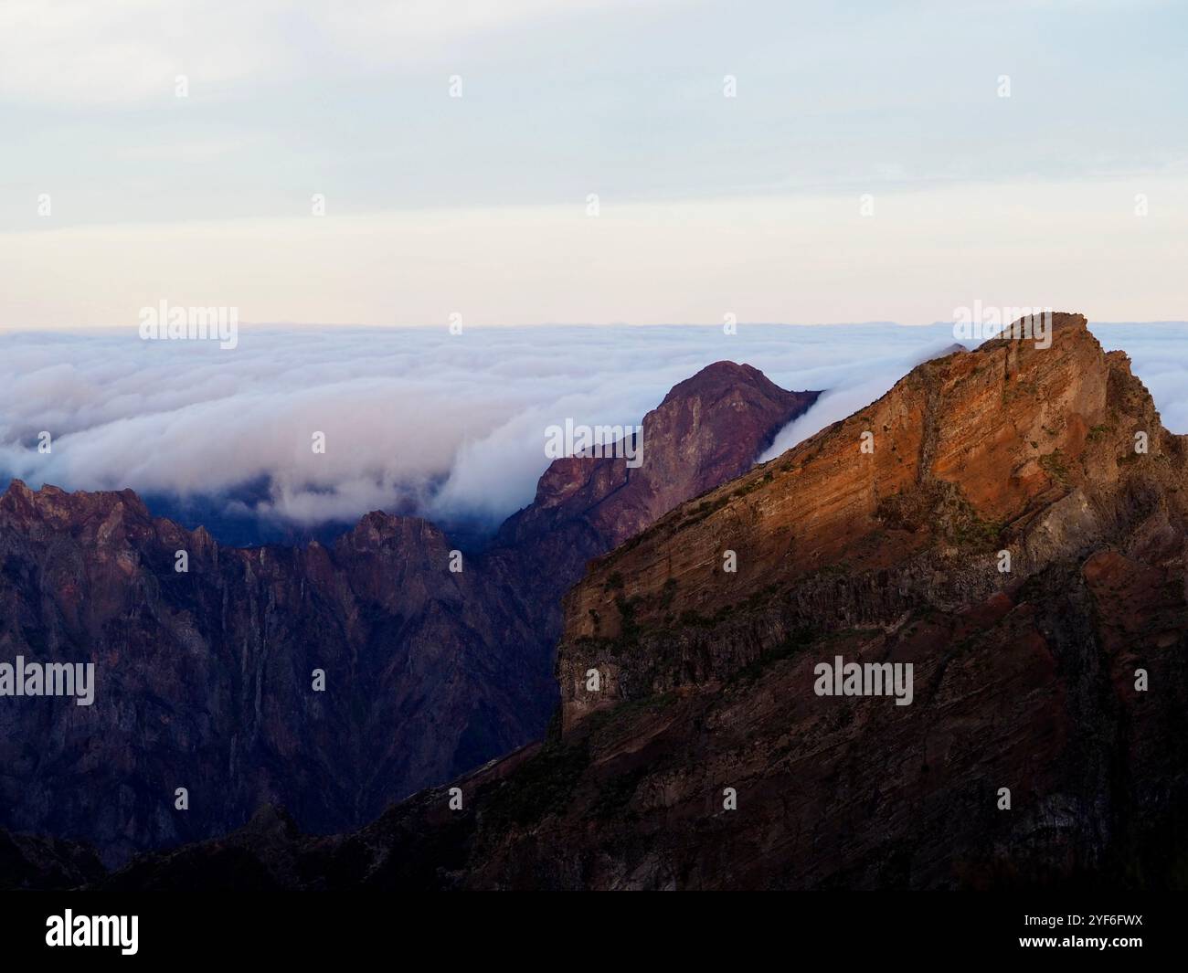 Sharp mountain peaks pierce through a thick flow of clouds as twilight ...
