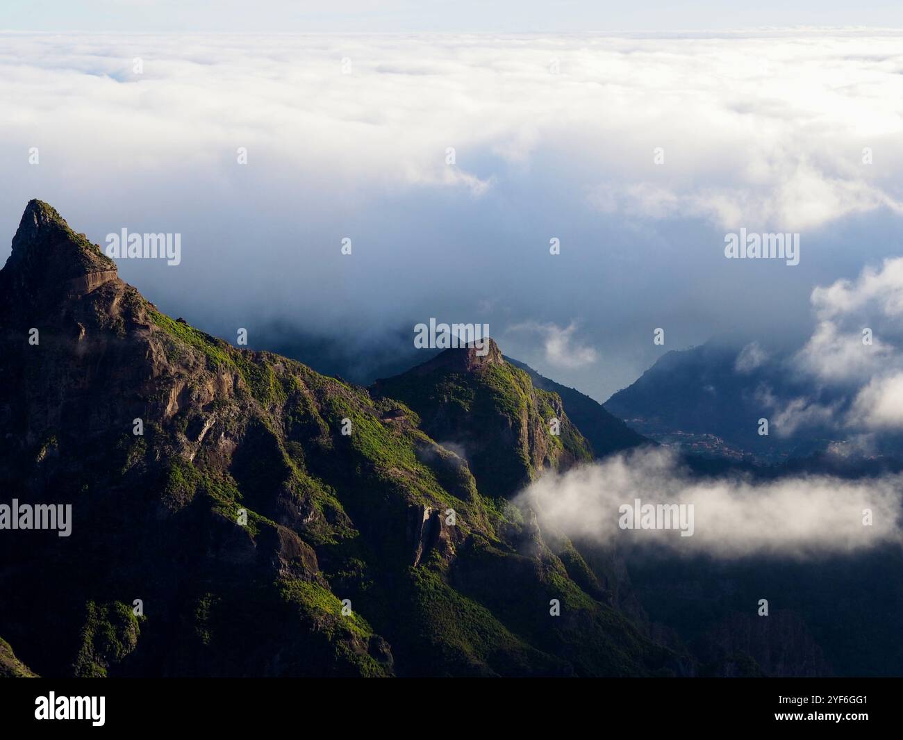 A dramatic mountain peak towers into a sky filled with clouds, creating ...