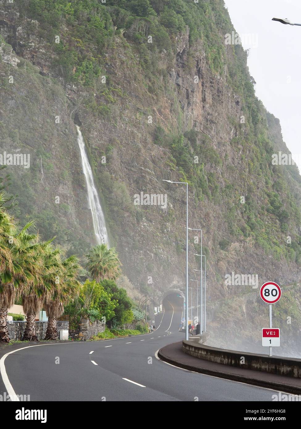 A curving road leads past a cascading waterfall and into a tunnel cut ...