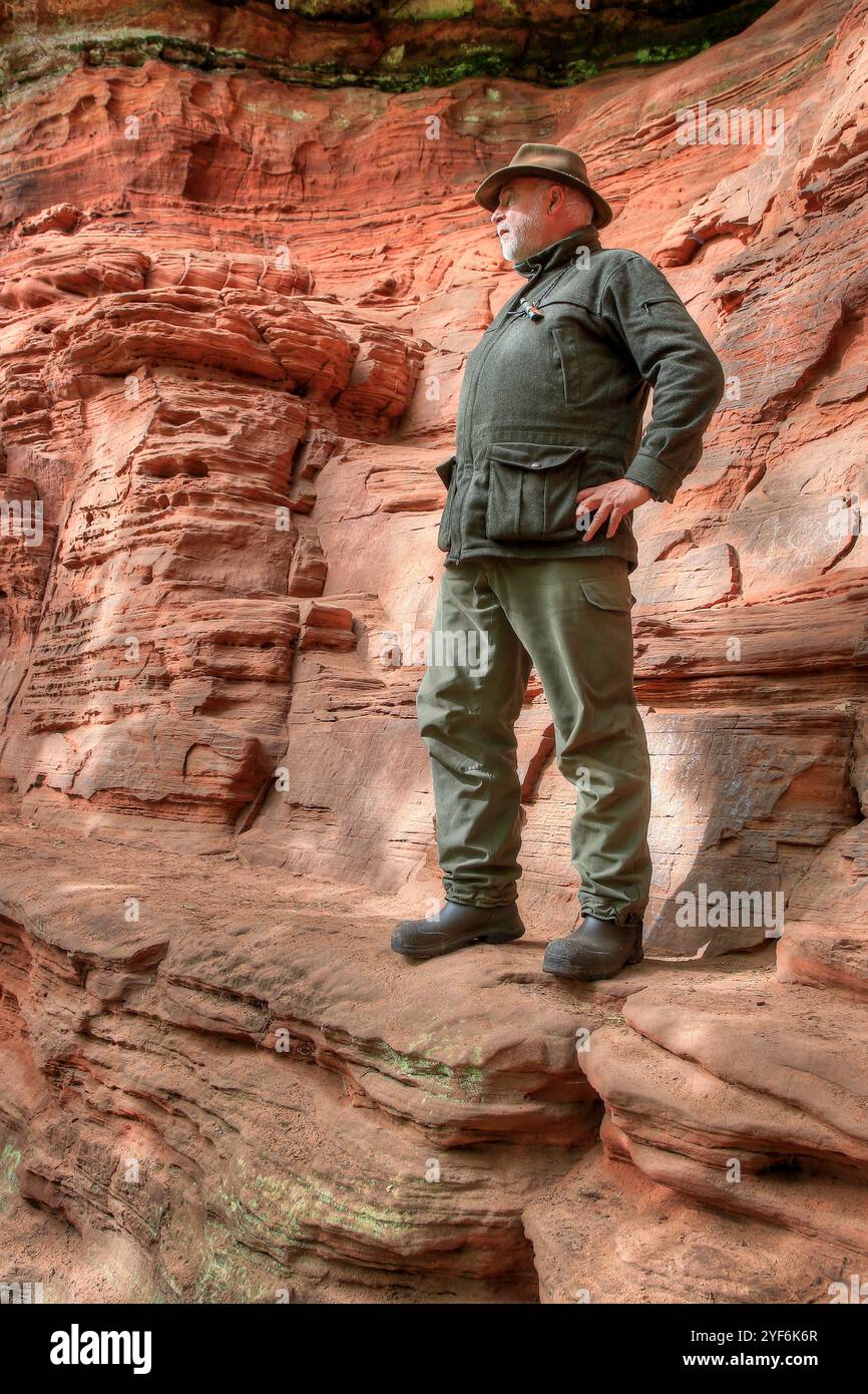 A senior hiker stands at the edge of a narrow rocky path, with a steep ...