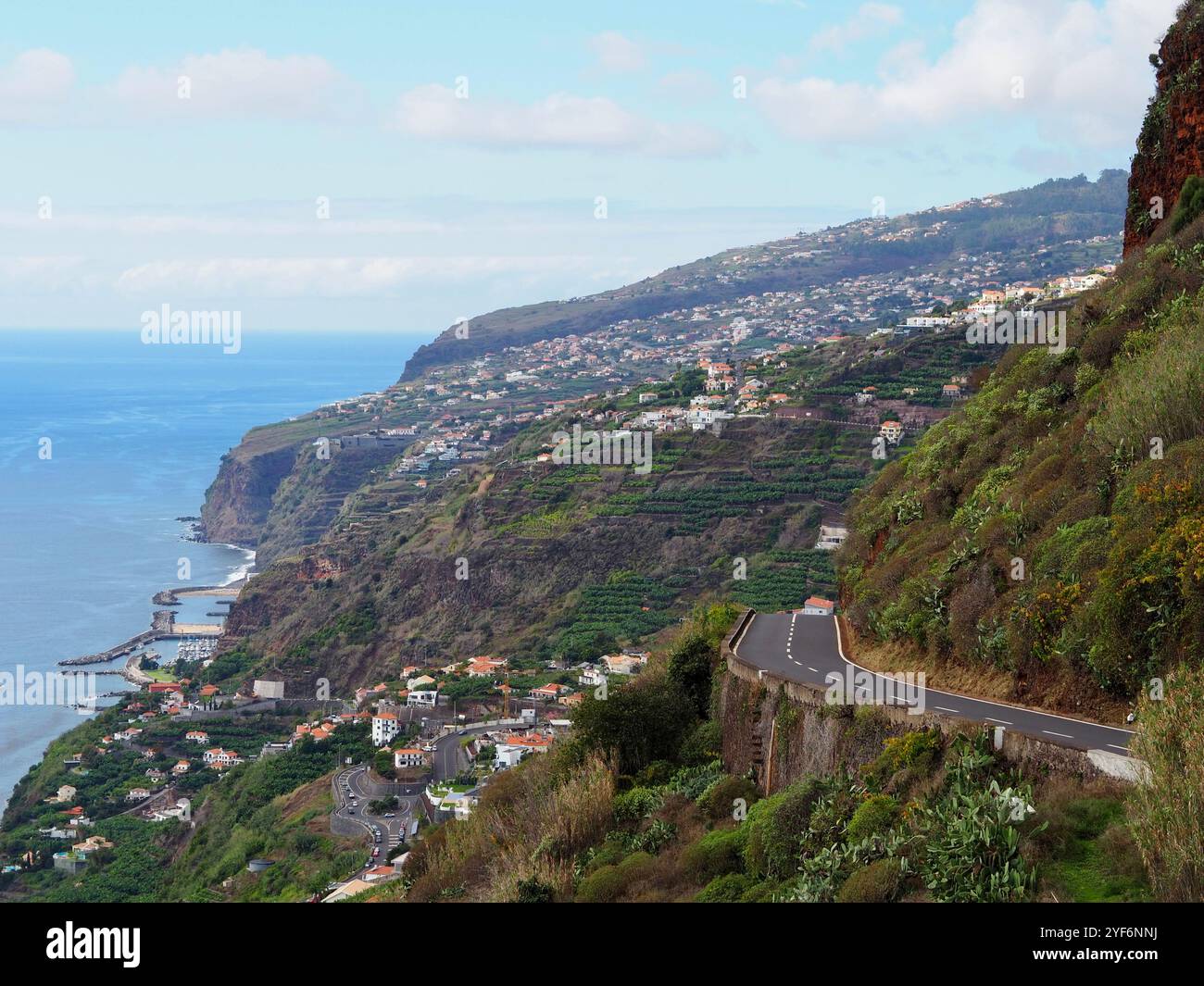 A scenic coastal road stretches along hills with houses and vegetation ...