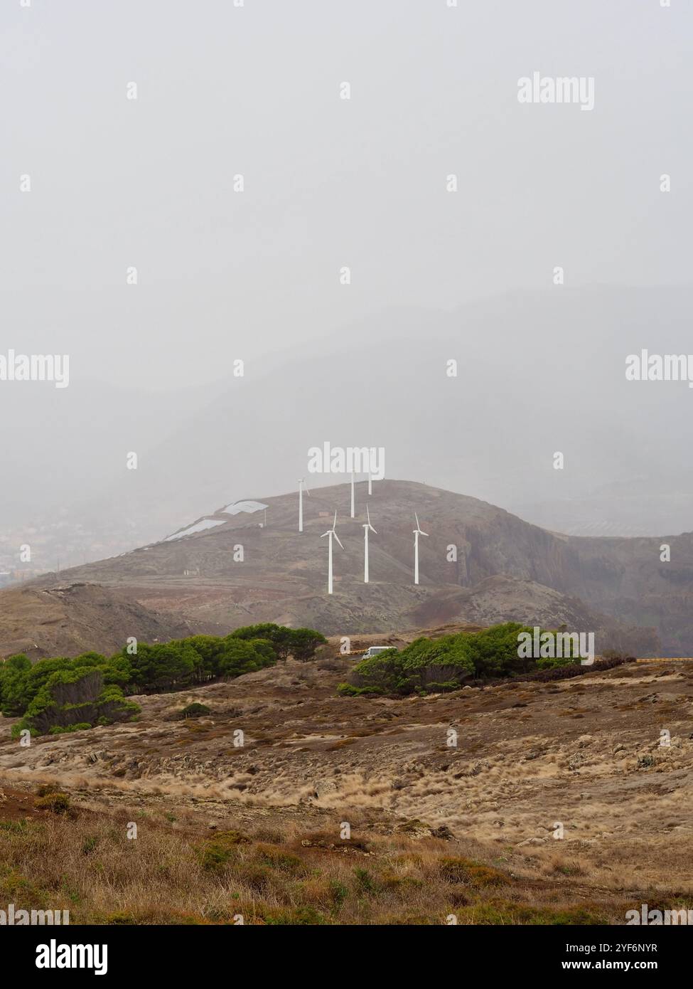The image showcases wind turbines on a foggy hill, surrounded by sparse ...