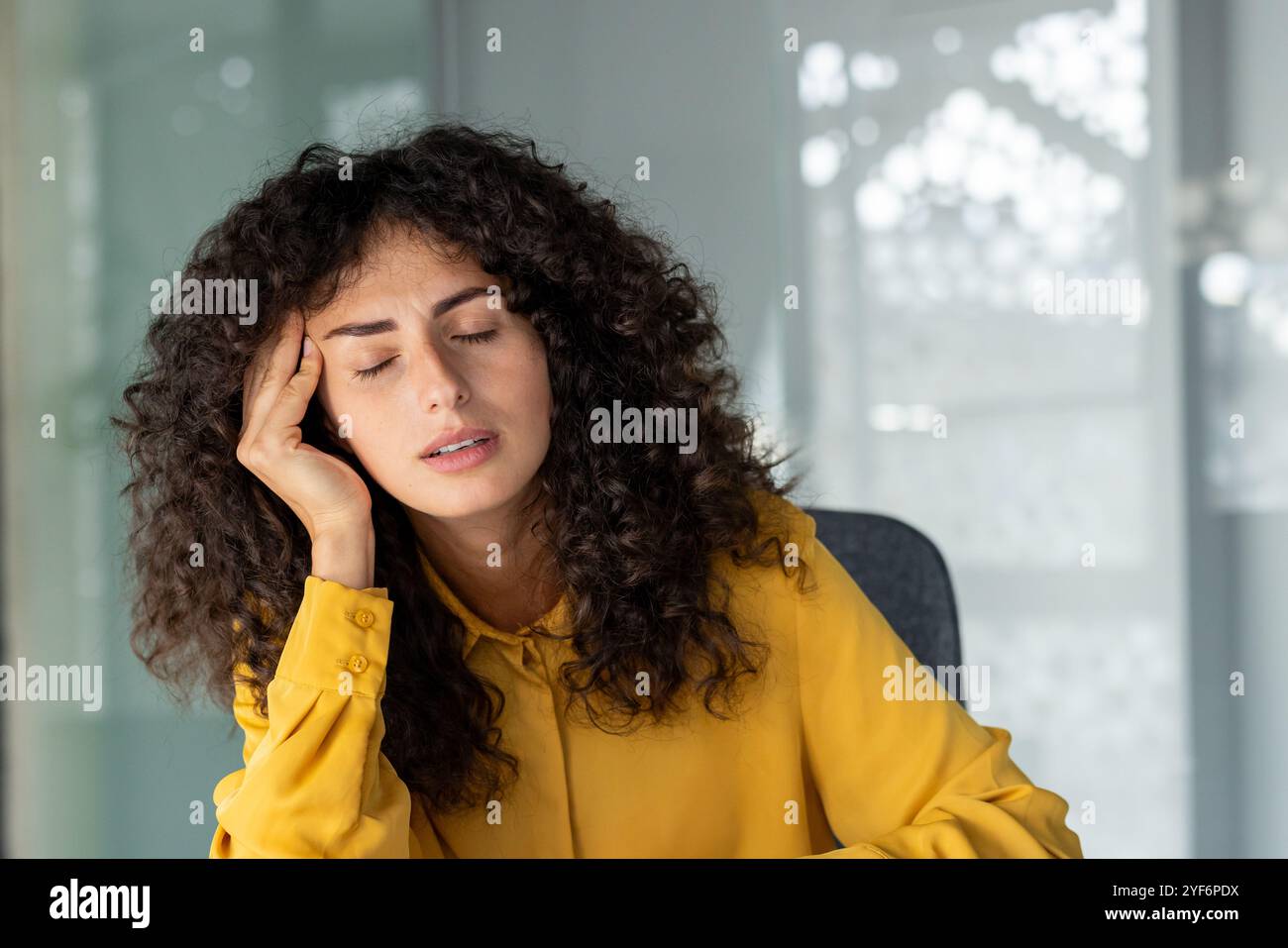 Businesswoman in yellow top sitting at desk showing signs of stress and ...