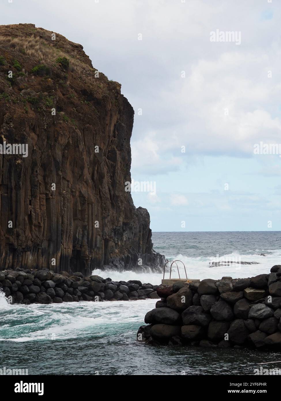 A striking image of a towering rocky cliff face beside the ocean, with ...