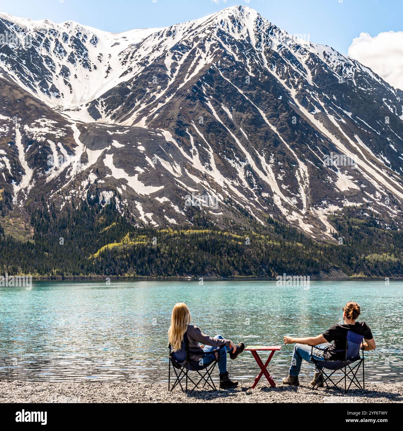 Two people, friends, couple sitting on camping chairs with picnic table ...
