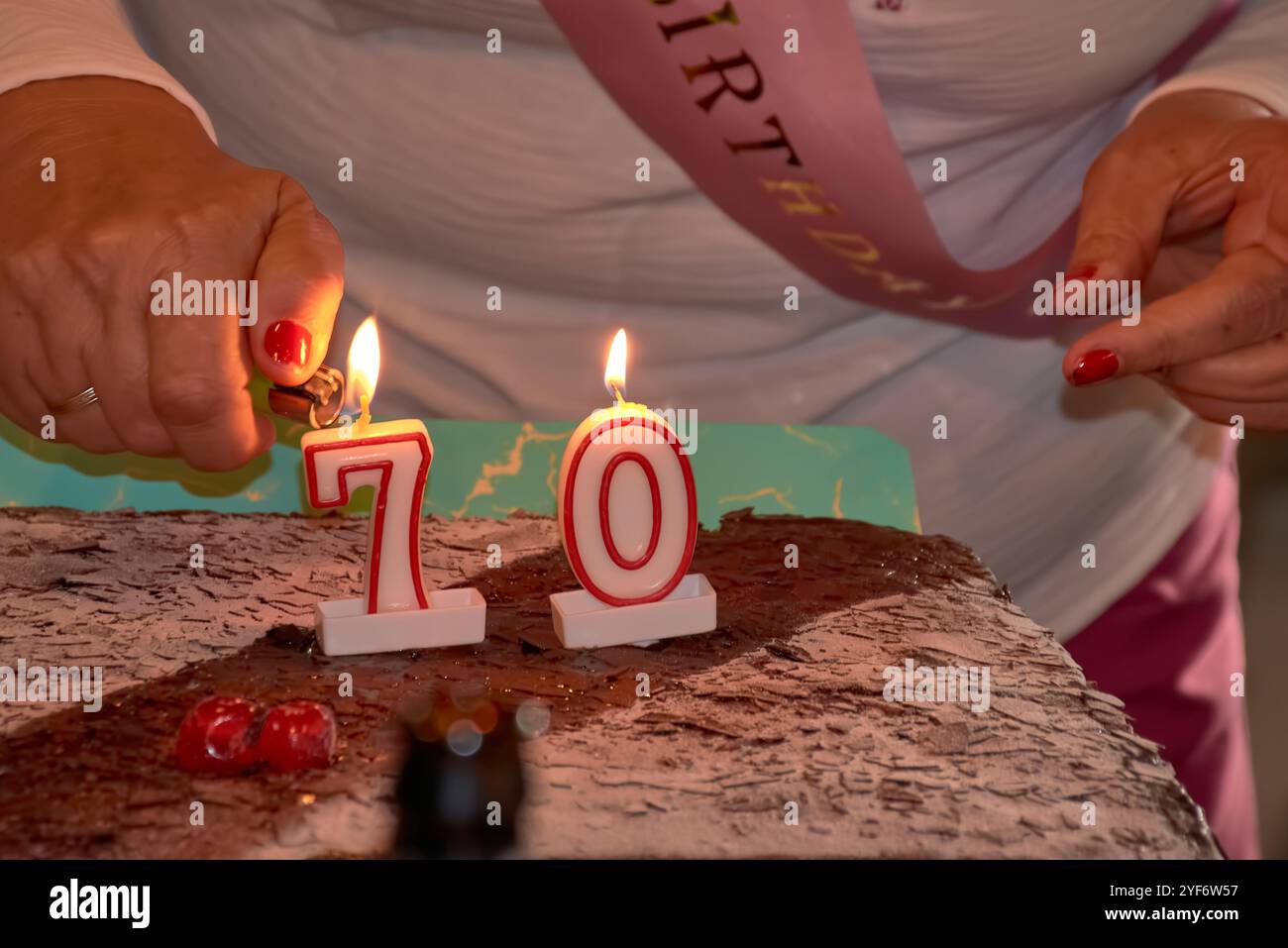 A close-up shot of a woman lighting a 70th birthday candle on a cake ...