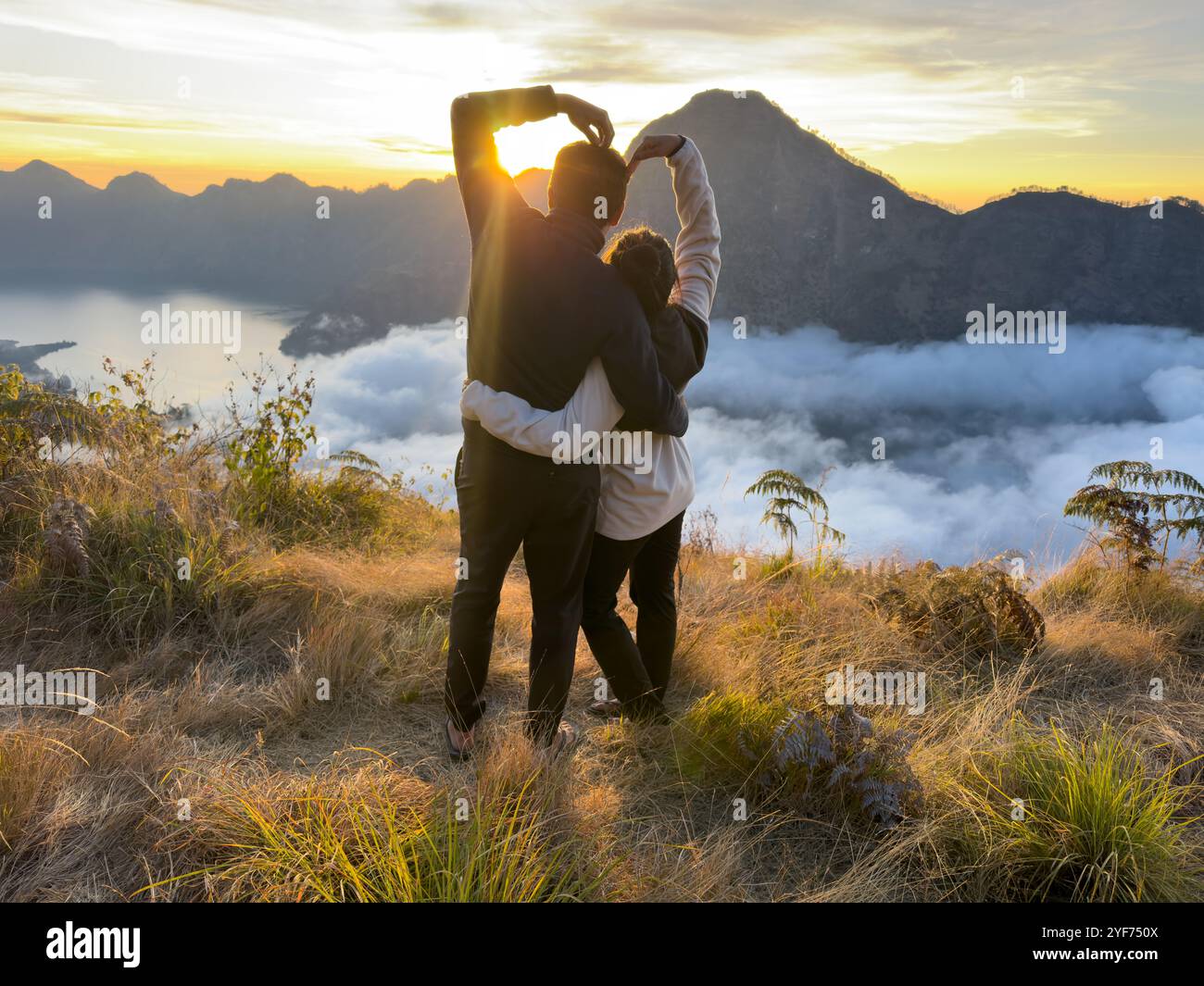 Rear view of a Couple making a heart sign while watching the sunset on ...