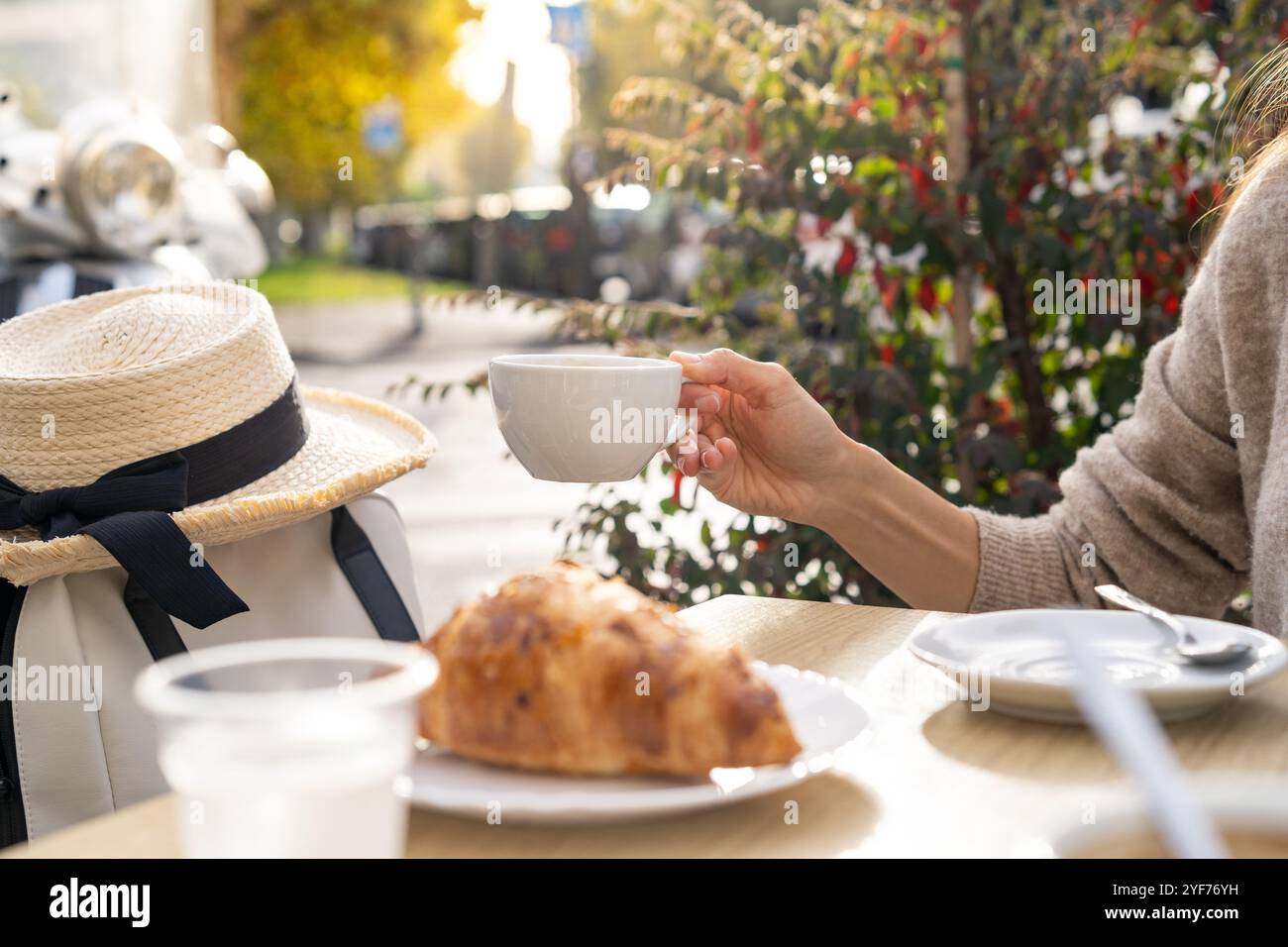 Woman sitting at an outdoor cafe enjoying a cup of coffee and almond ...