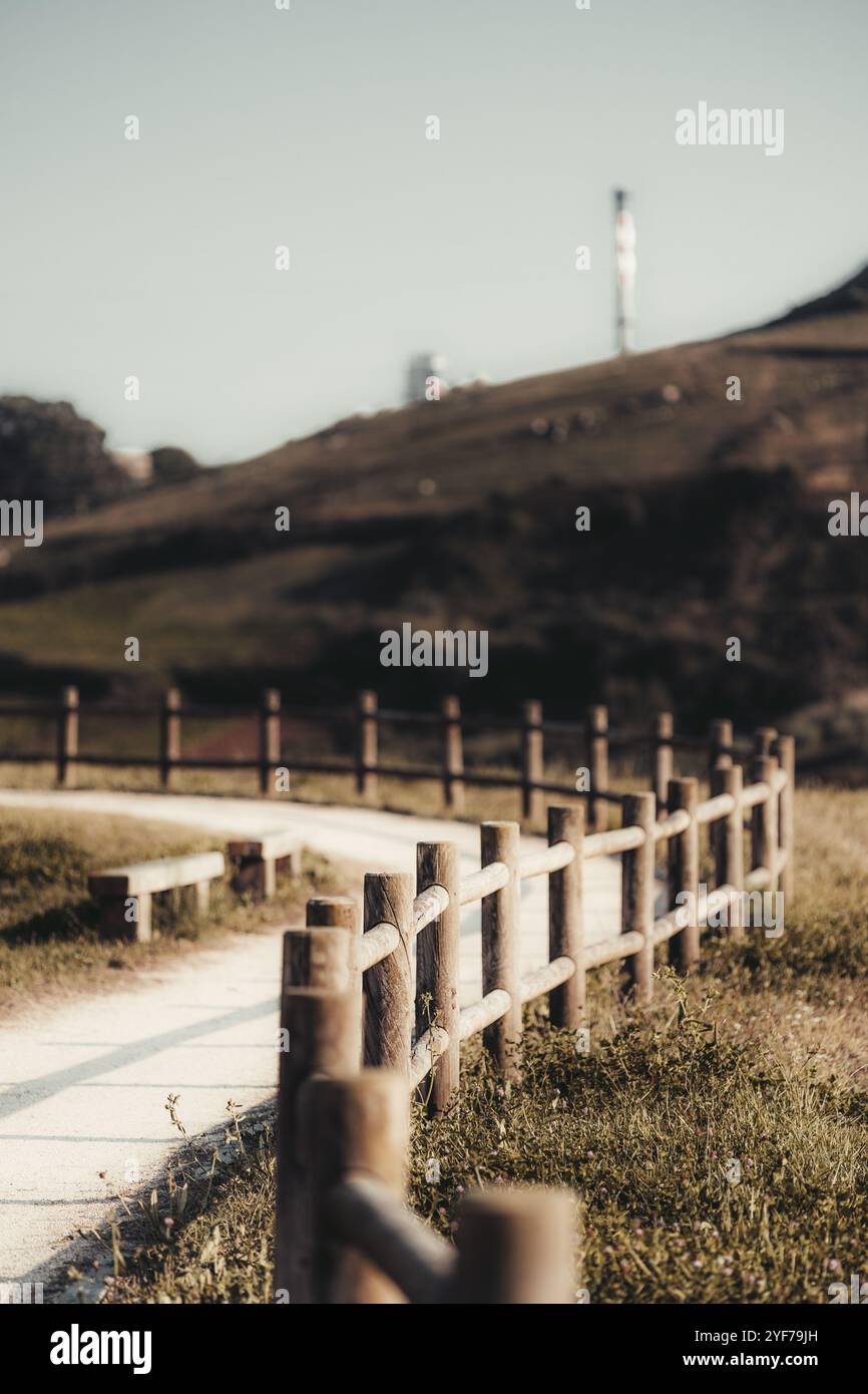 Vertical telephoto shot of a wooden fence lines a winding gravel pathway across a grassy ...