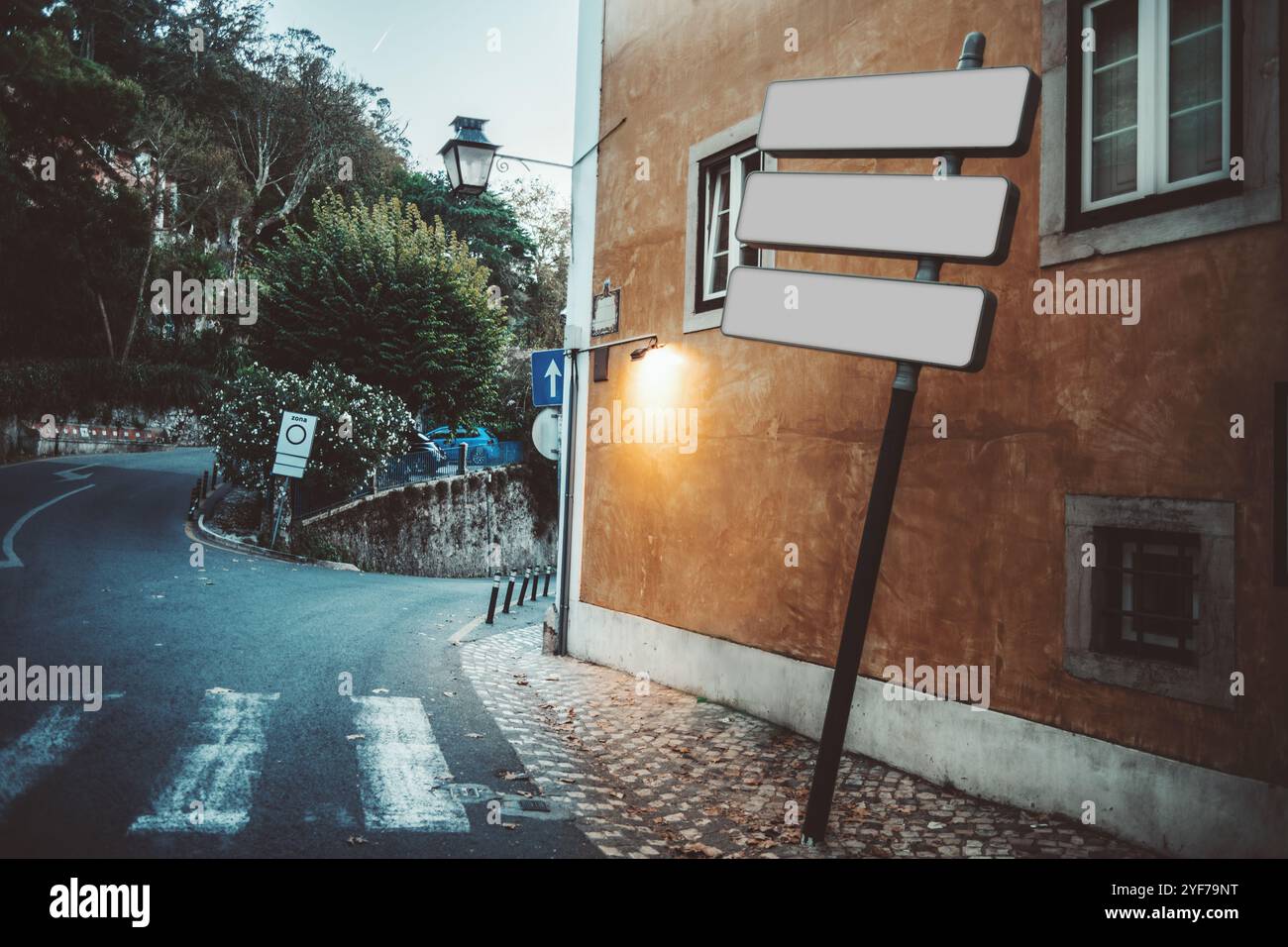 A street with an empty three-panel sign mockup on a leaning pole next ...