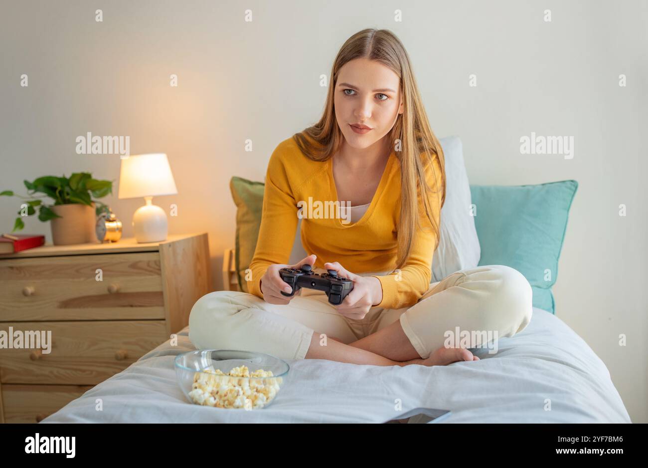 Teen girl playing video games on her bed while enjoying popcorn in her ...