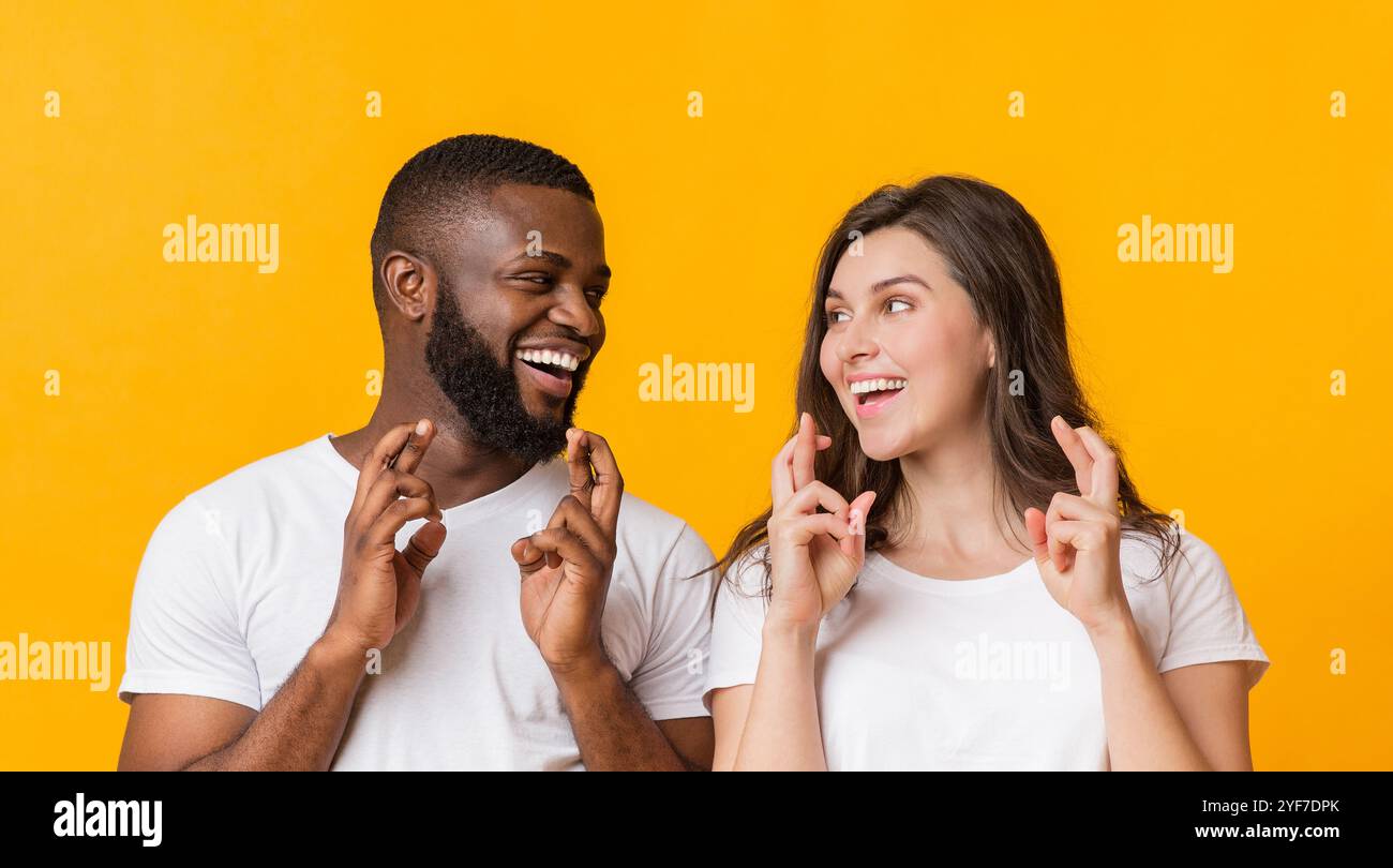 Cheerful interracial couple making wish, pleading for something with ...