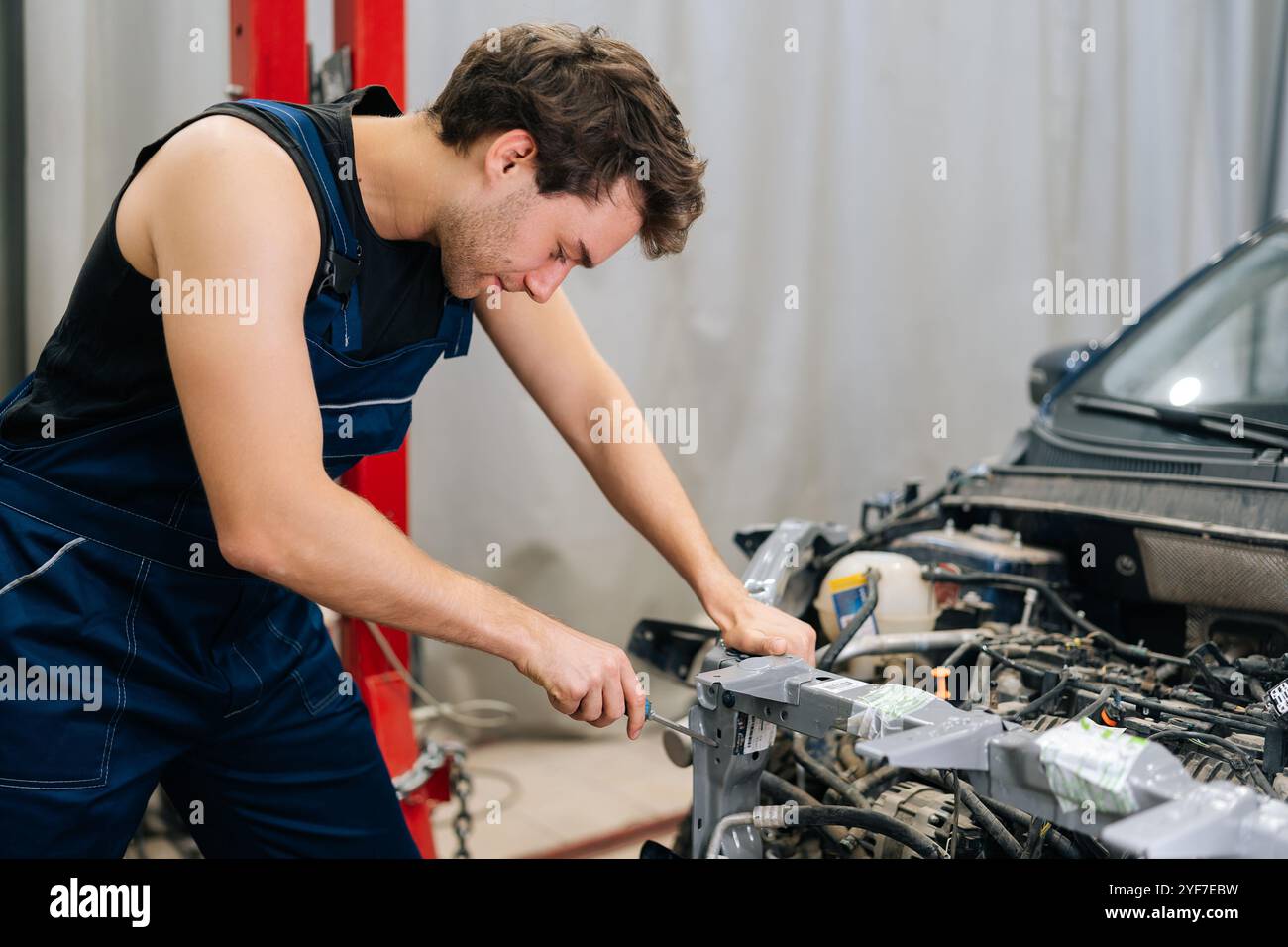 Side view of mechanic male wearing blue overalls working under hood of ...