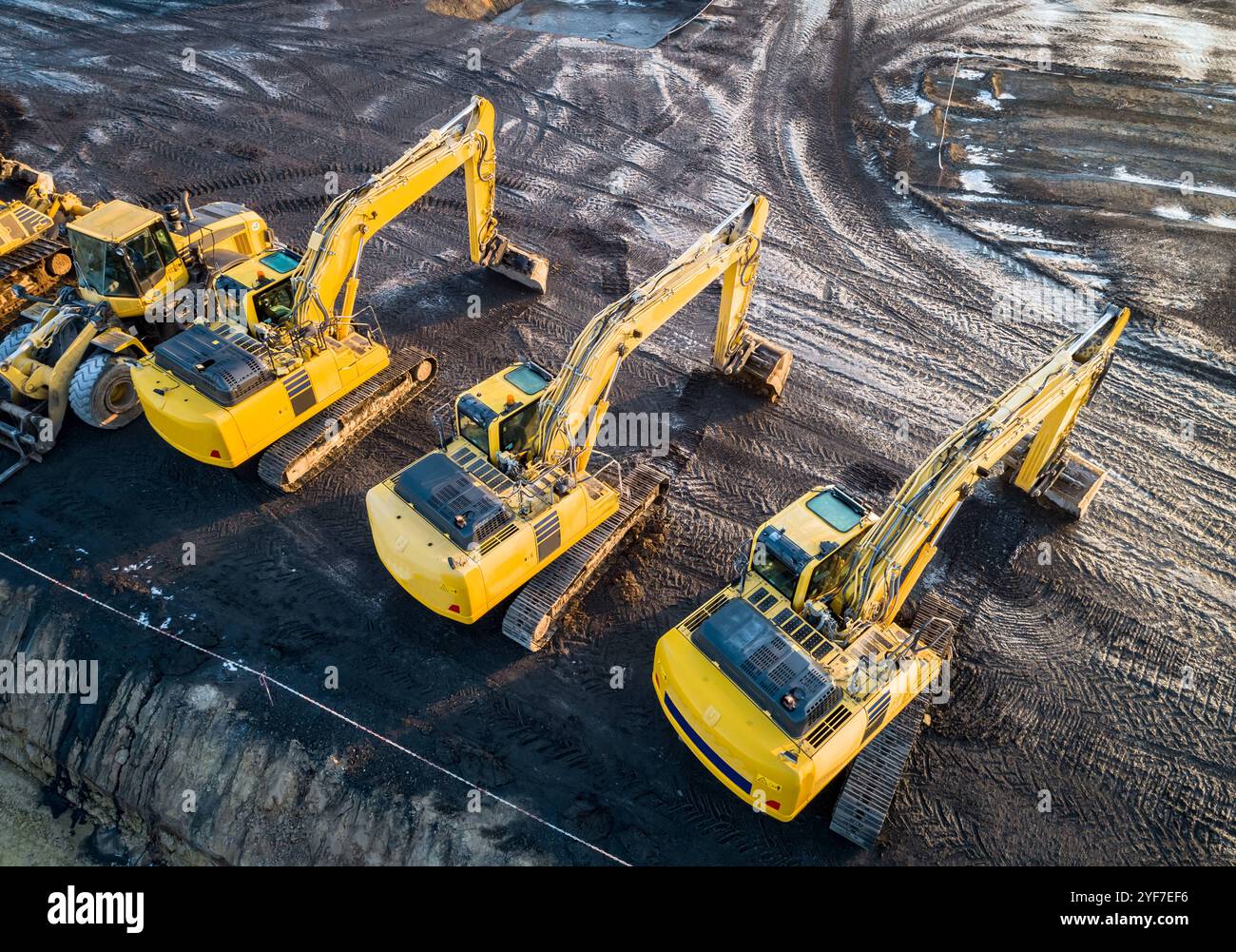 Großbaustelle - aufgereihte, gelbe Bagger parken neben dem Rohbau einer ...