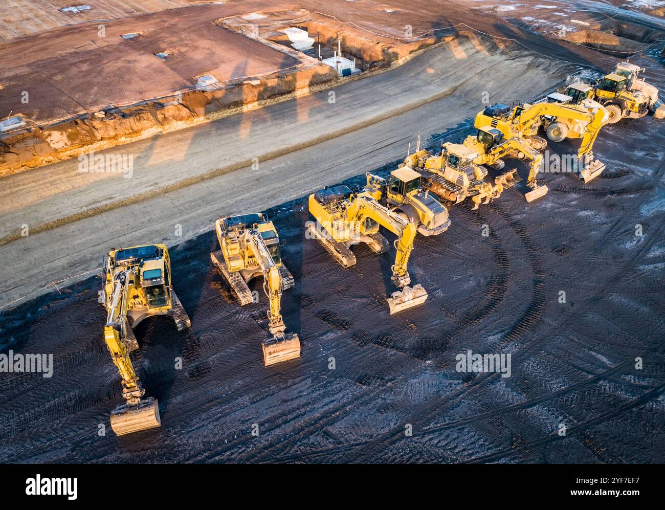 Großbaustelle - aufgereihte, gelbe Bagger parken neben dem Rohbau einer ...