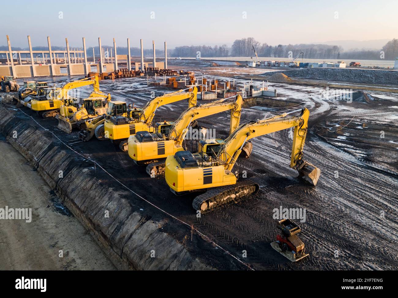 Großbaustelle - aufgereihte, gelbe Bagger parken neben dem Rohbau einer ...