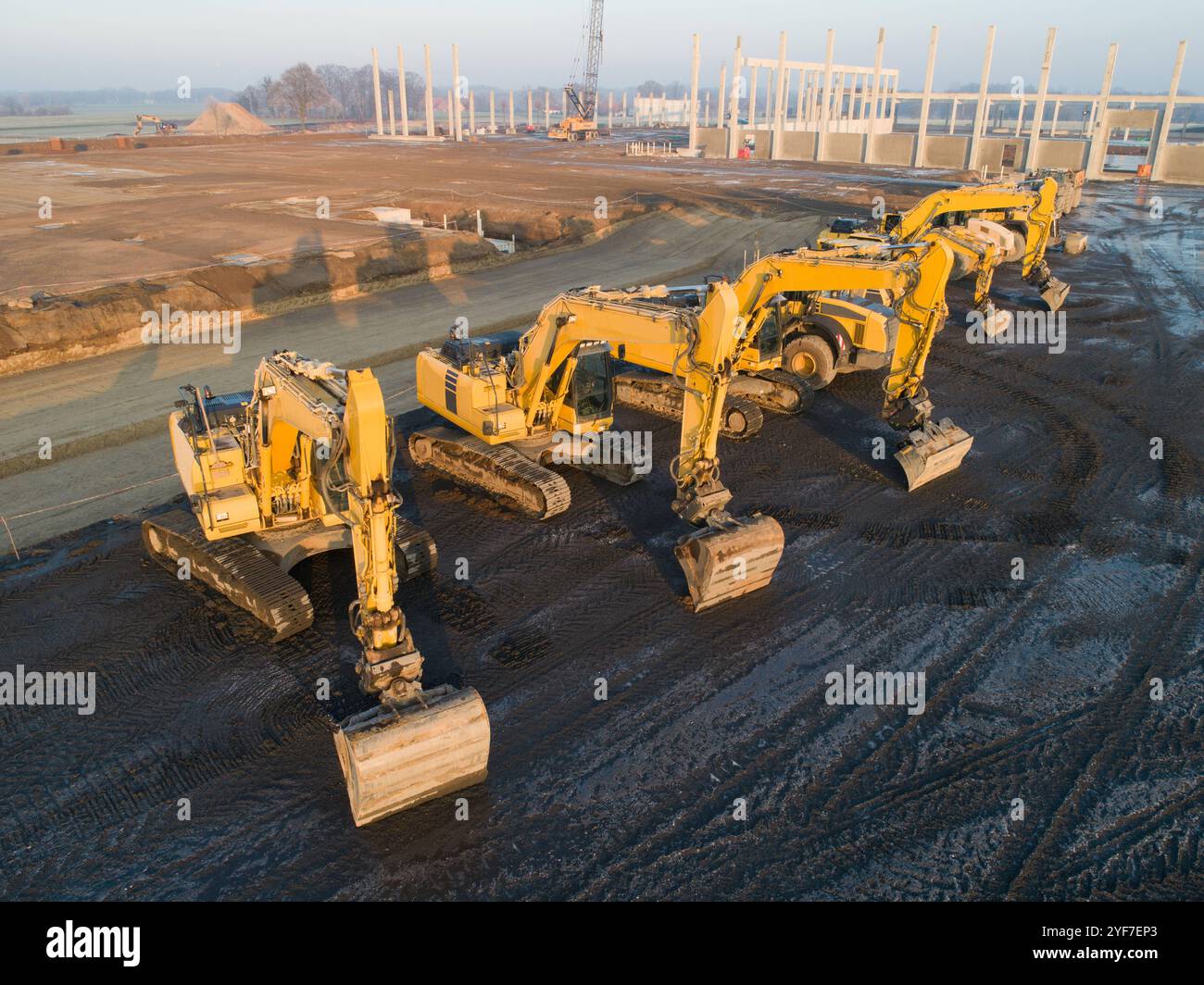 Großbaustelle - aufgereihte, gelbe Bagger parken neben dem Rohbau einer ...