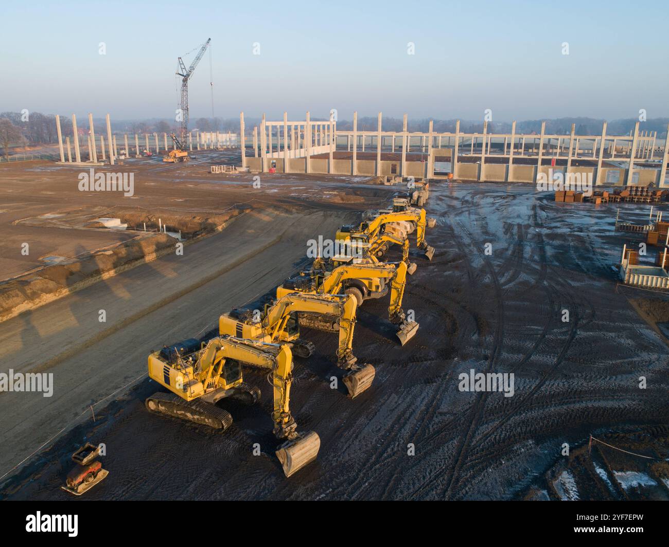 Großbaustelle - aufgereihte, gelbe Bagger parken neben dem Rohbau einer ...