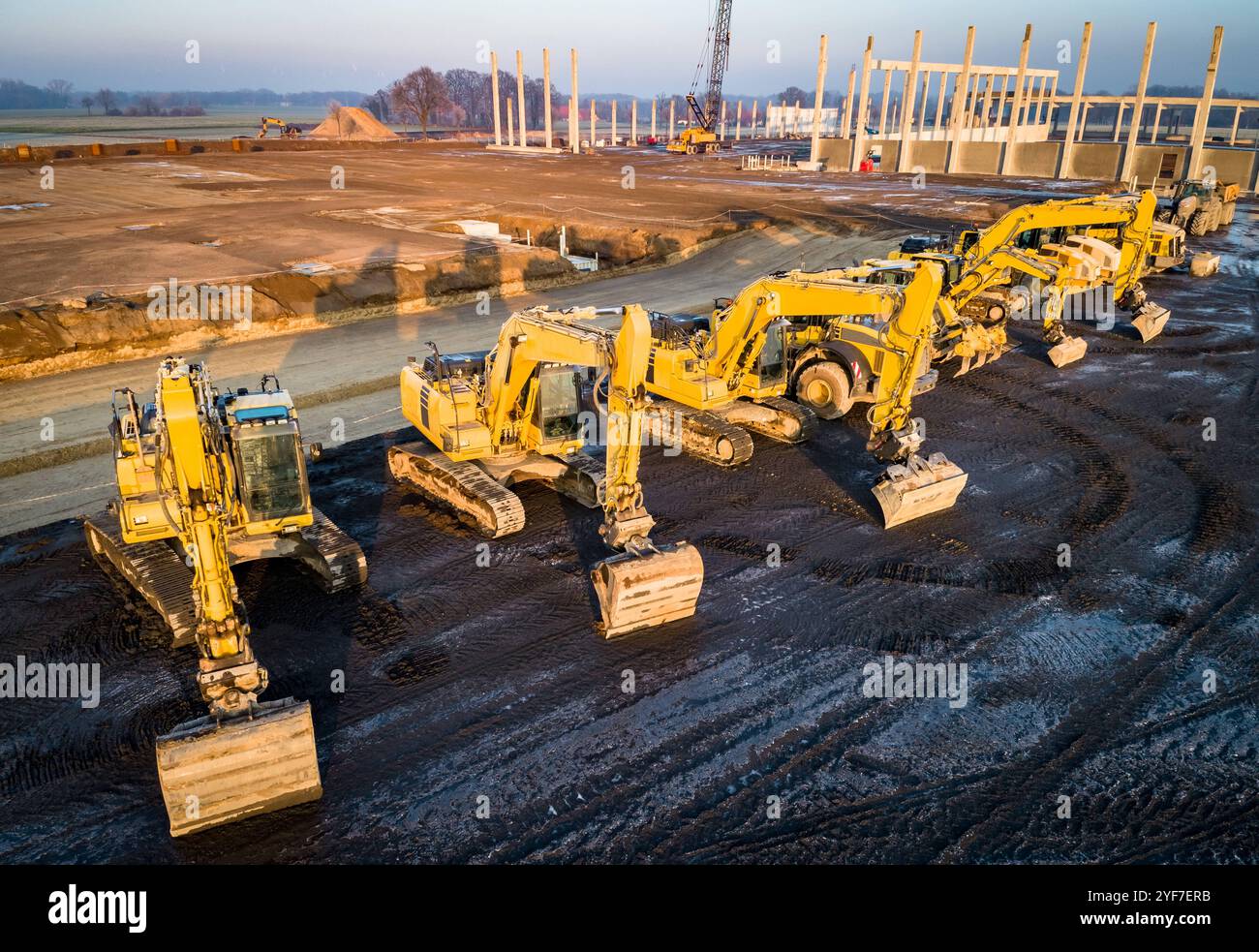 Großbaustelle - aufgereihte, gelbe Bagger parken neben dem Rohbau einer ...