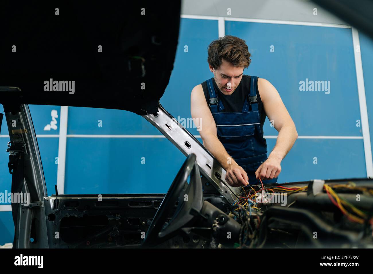 Focused mechanic in blue overalls repairing car electrical system in ...