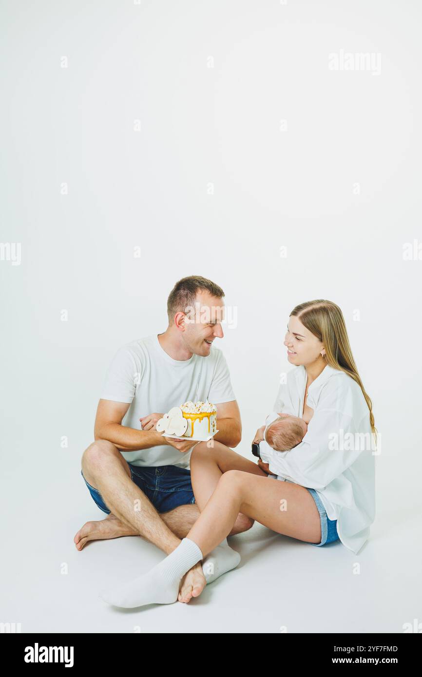 Young happy parents with a baby in their arms and a cake celebrate the ...