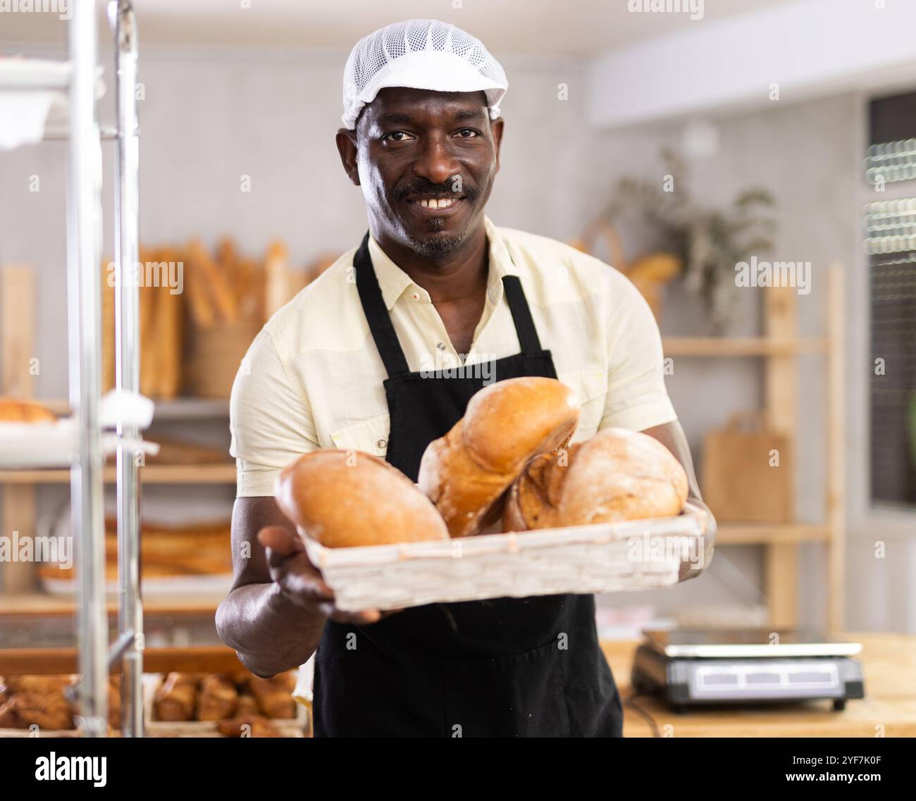 African male baker worker sells loaf of bread, shows many products ...